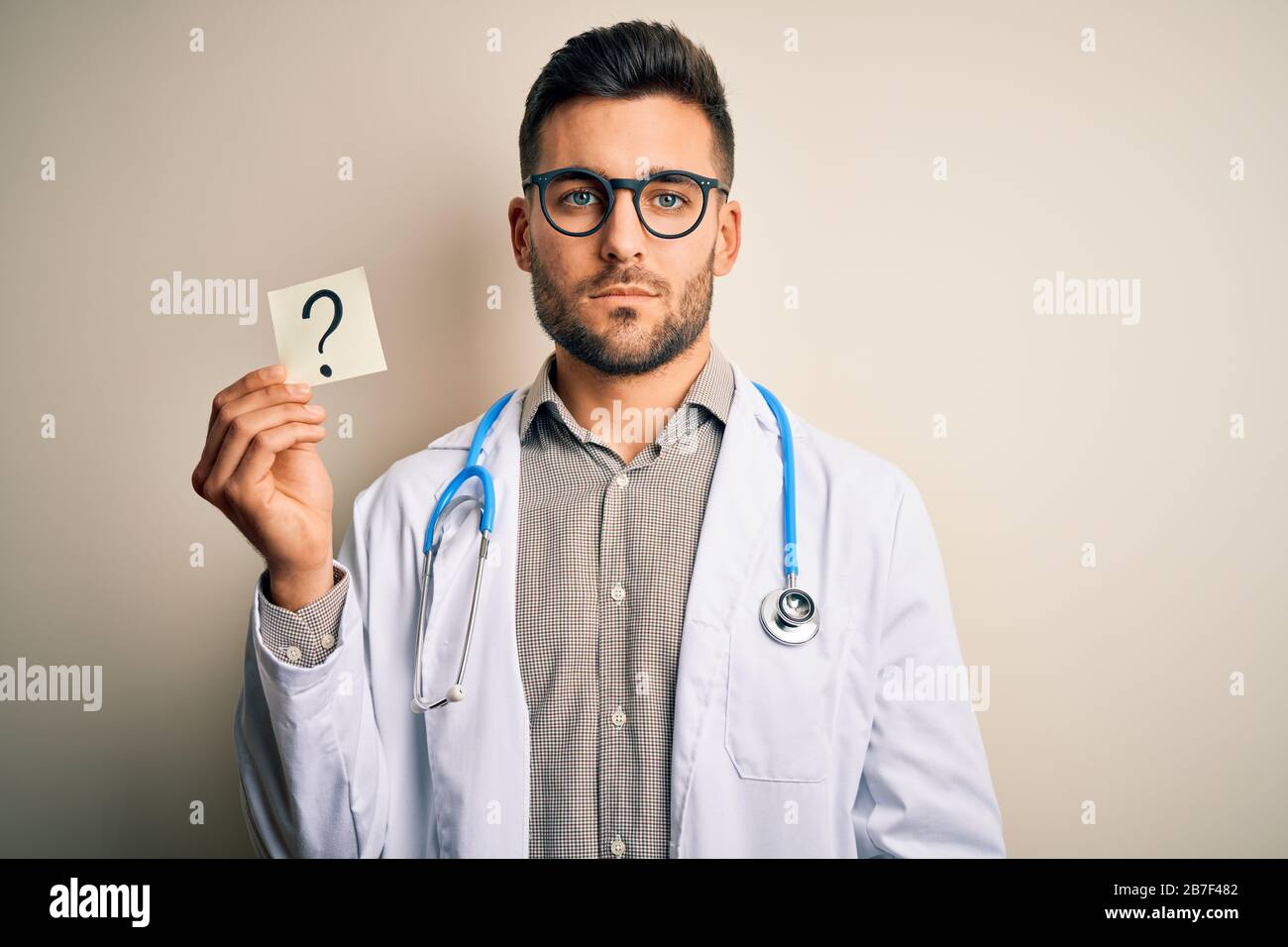 Young doctor man wearing stethoscope holding question mark reminder ...