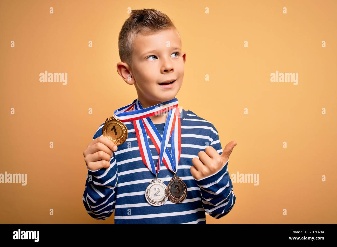 Young little caucasian winner kid wearing award competition medals over ...