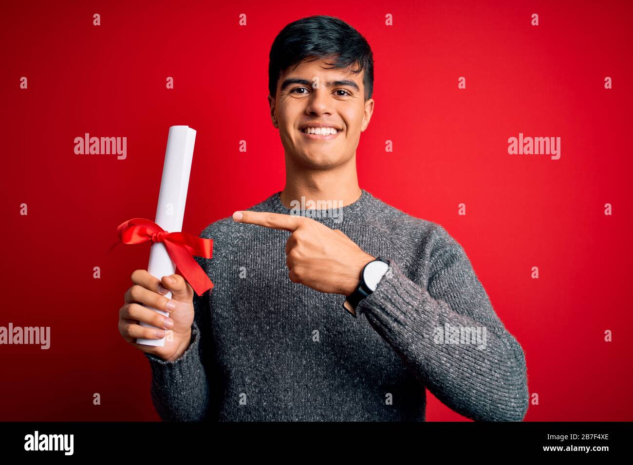 Young student man holding university graduated diploma degree over red ...