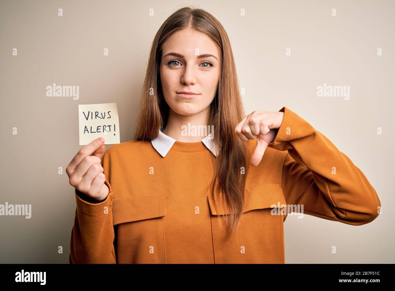 Young beautiful redhead woman holding reminder paper with virus alert ...