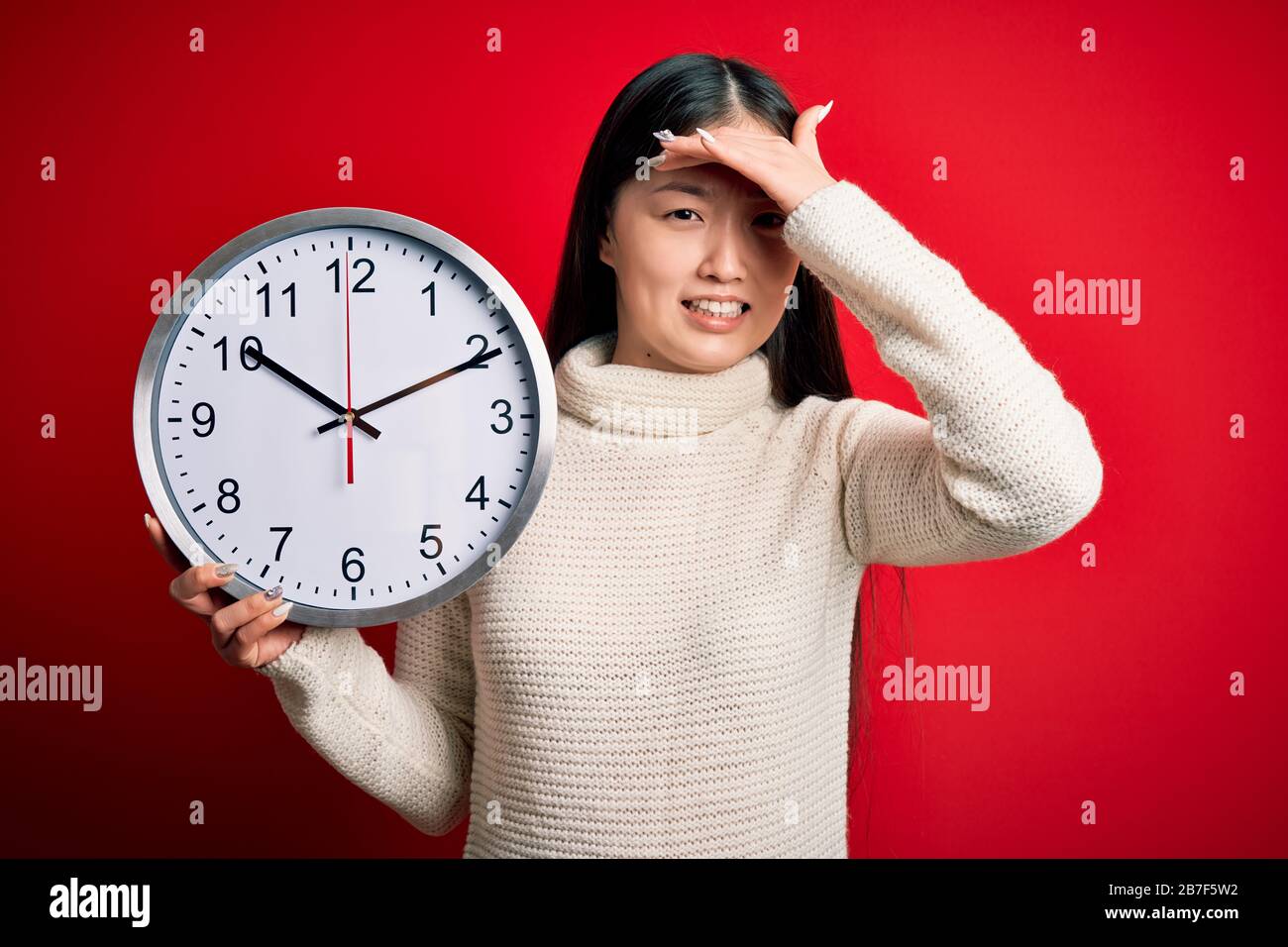 Young asian woman holding countdown big clock over red isolated ...