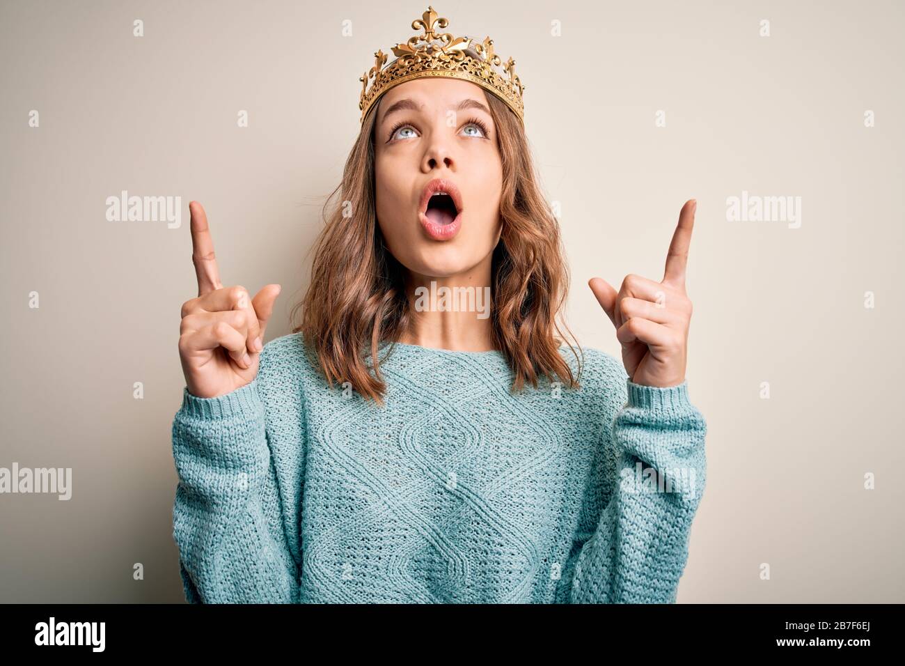 Young blonde girl wearing queen golden crown over isolated background ...