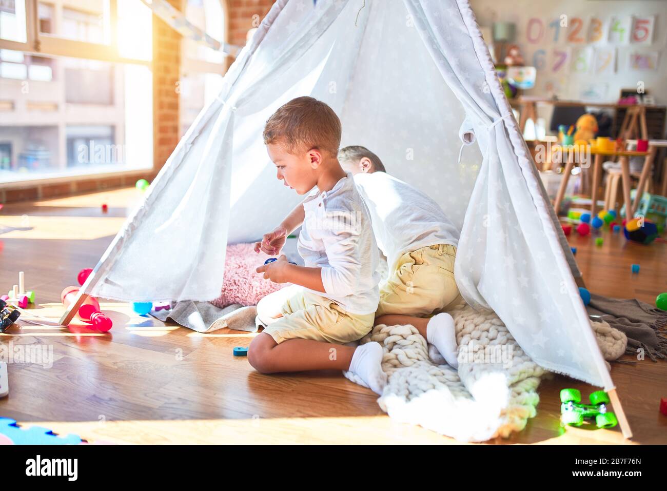 Adorable blonde twins playing inside tipi around lots of toys at ...