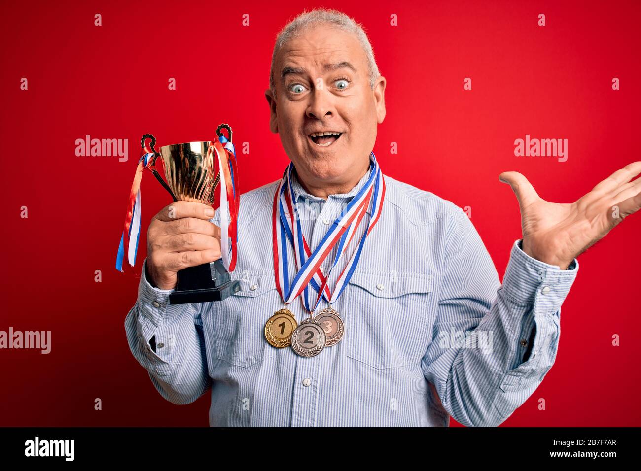 Middle age hoary successful man wearing medals holding trophy over ...