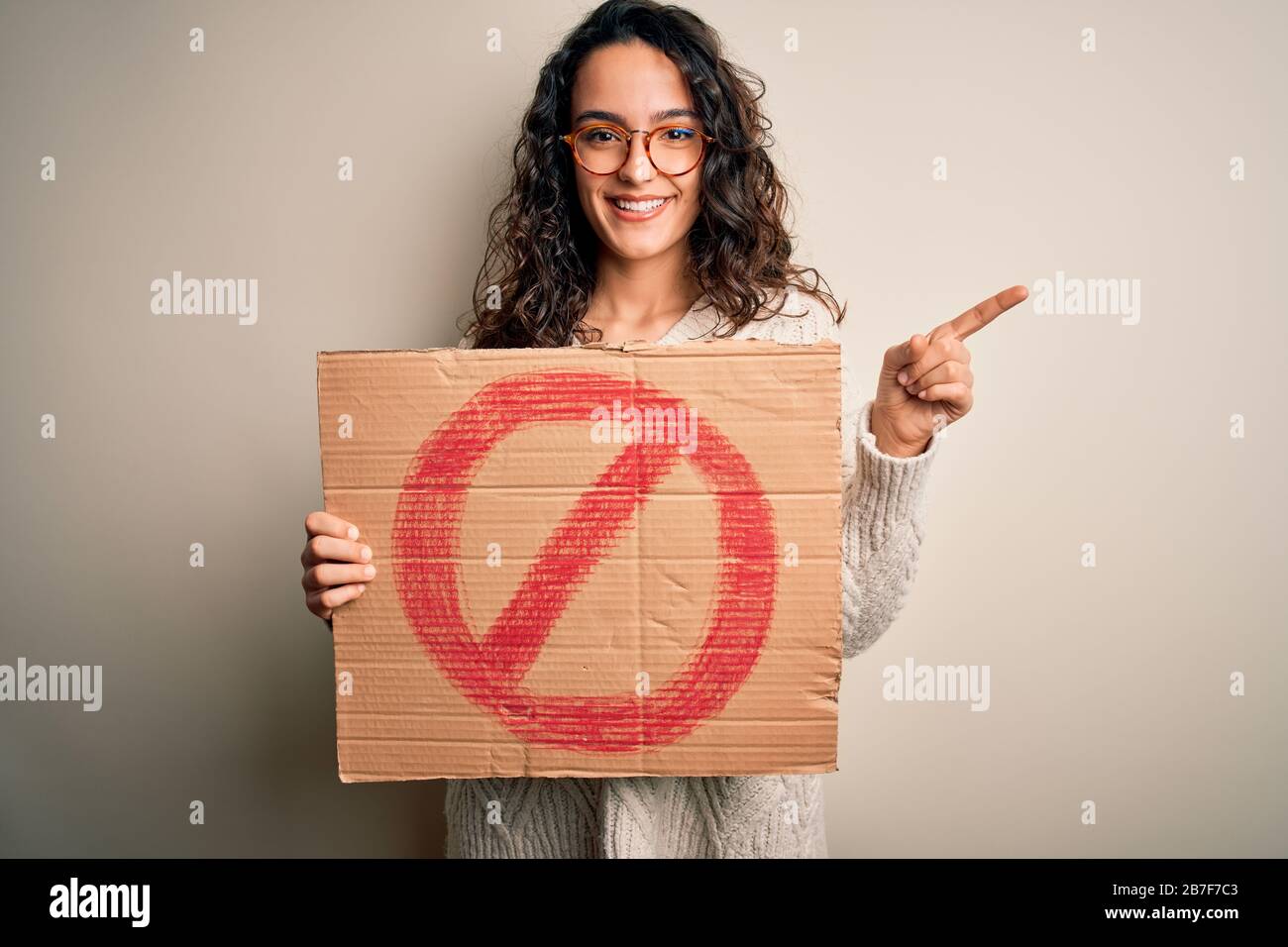 Young beautiful woman with curly hair holding banner with prohibited ...