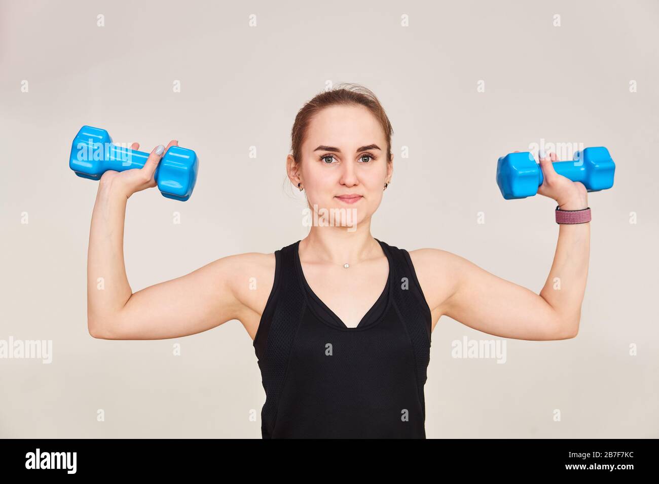 young petite woman performs an exercise with dumbbells, half-length ...