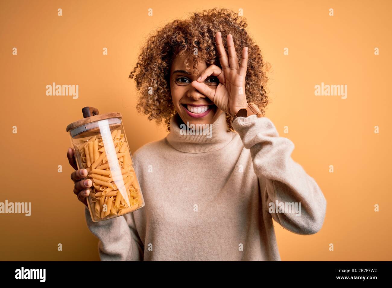 Young african american curly woman holding jar with Italian dry pasta ...