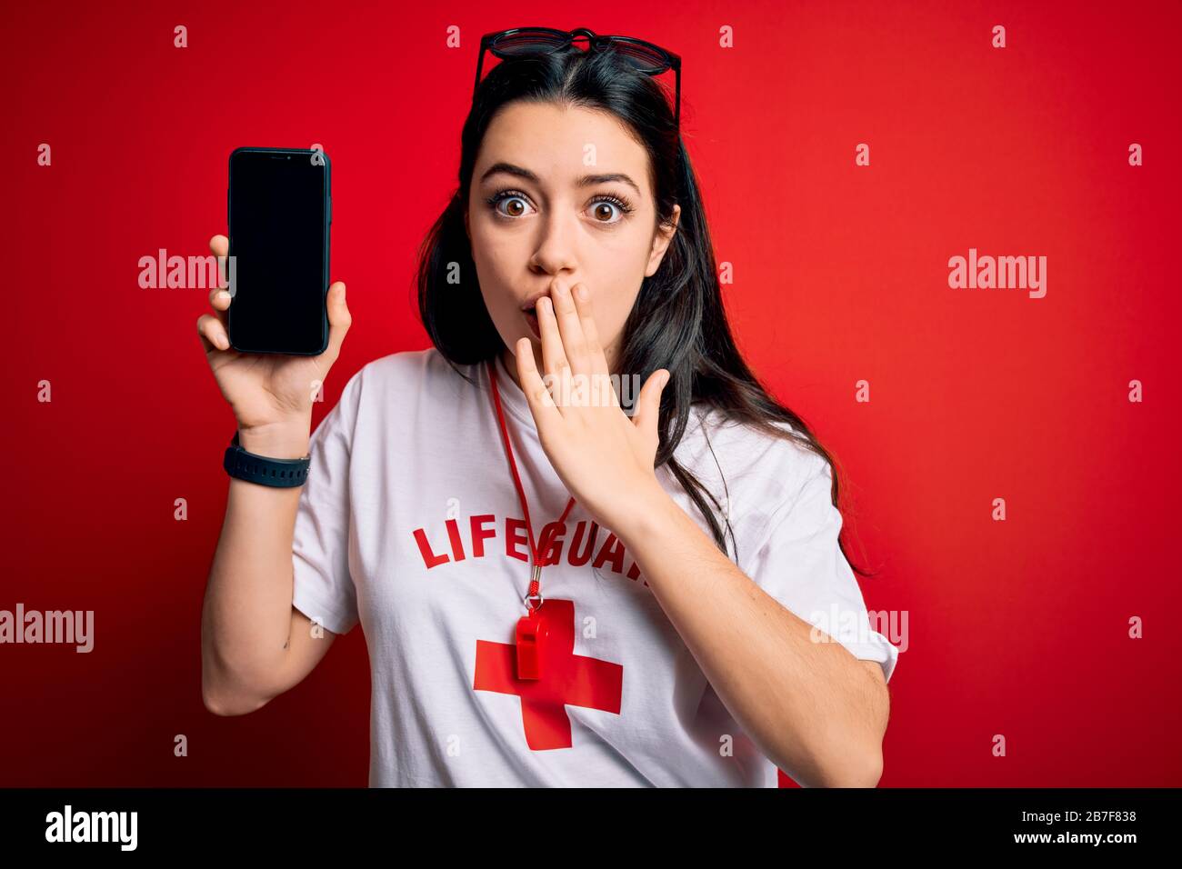 Young lifeguard woman showing smartphone screen over red background ...