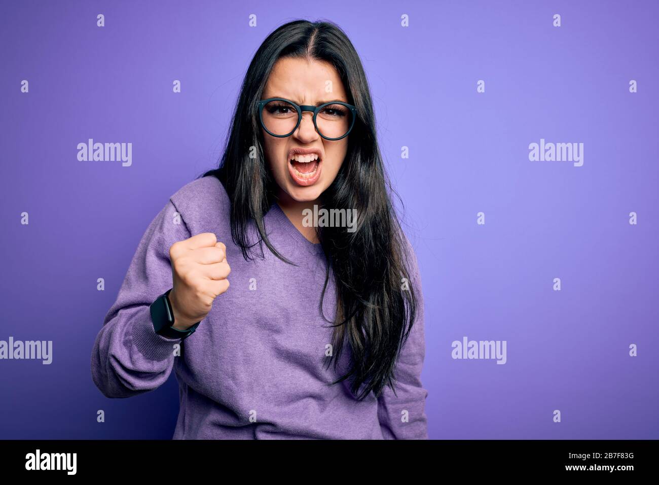 Young brunette woman wearing glasses over purple isolated background ...