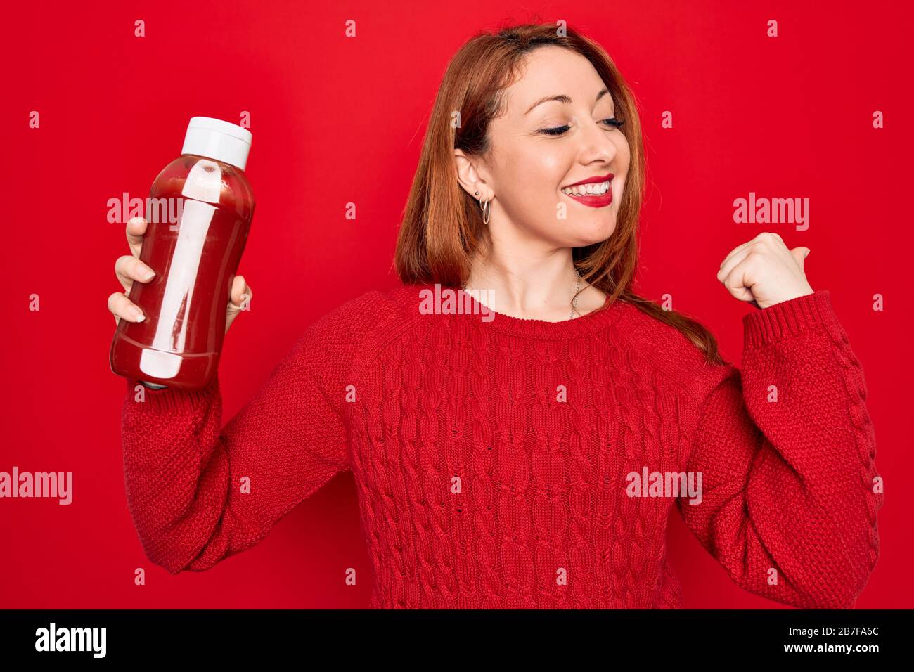 Beautiful redhead woman holding bottle of ketchup sauce condiment over ...