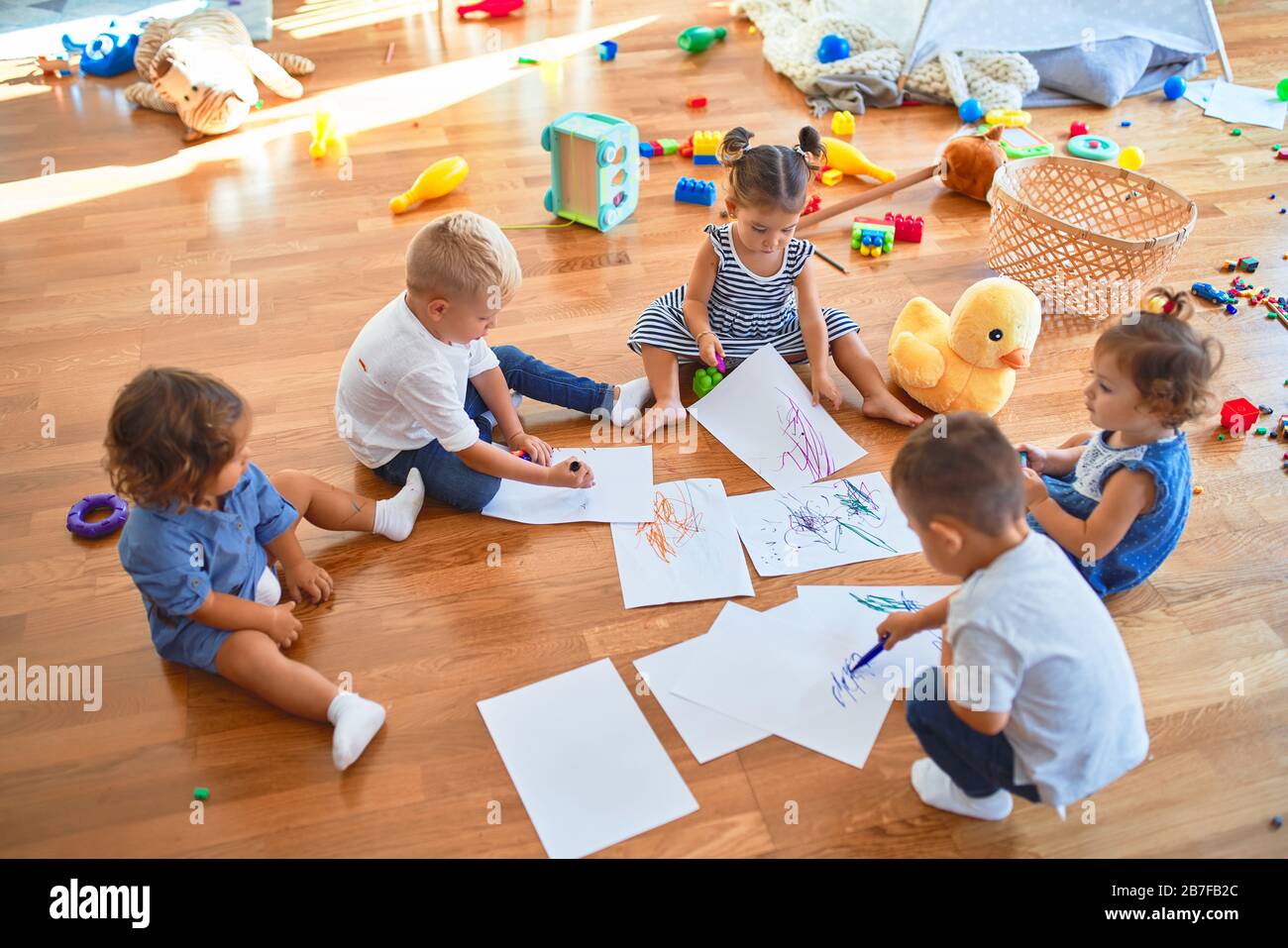 Adorable group of toddlers sitting on the floor drawing using paper and ...