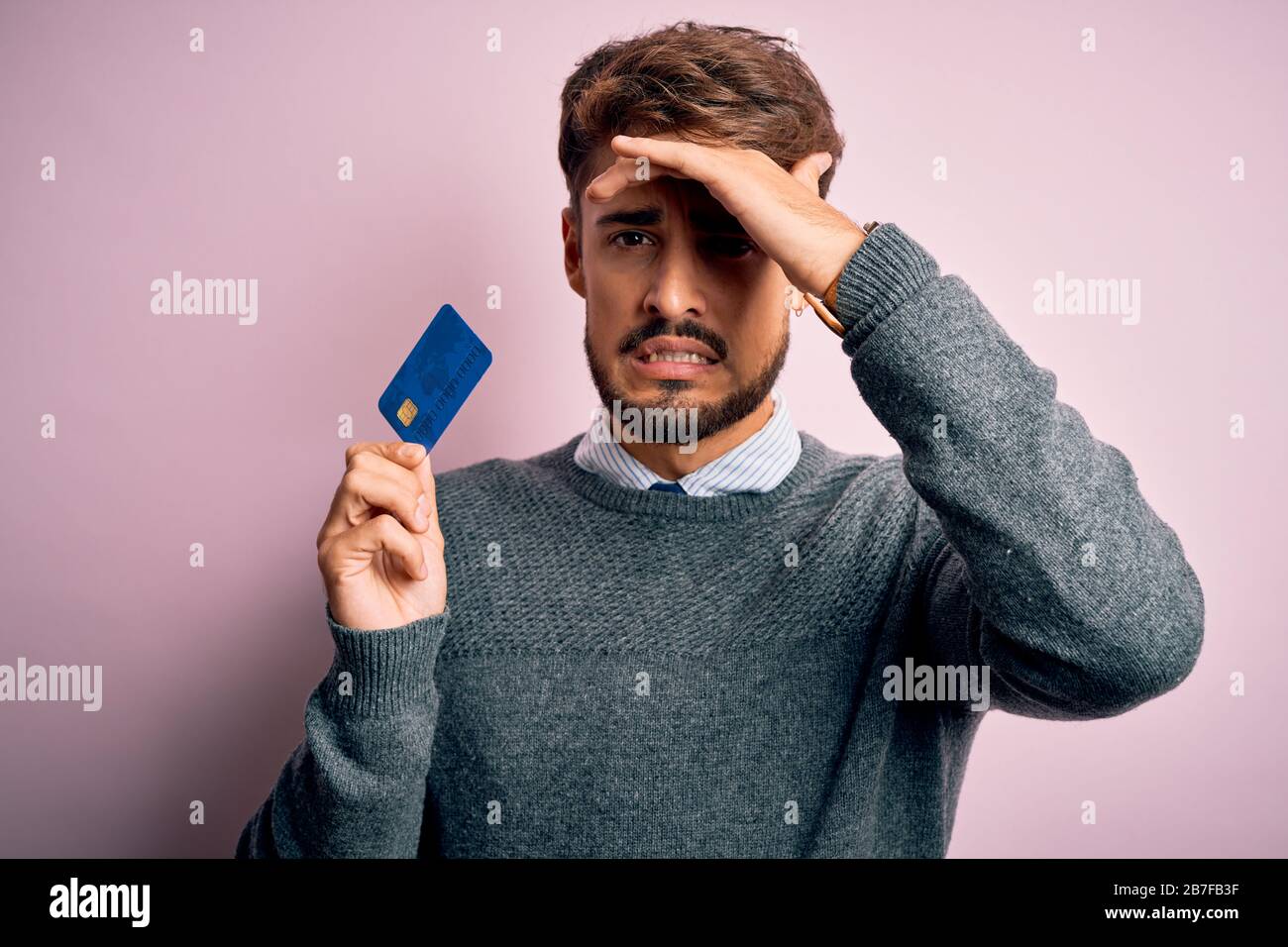 Young customer man with beard holding credit card for payment over pink ...