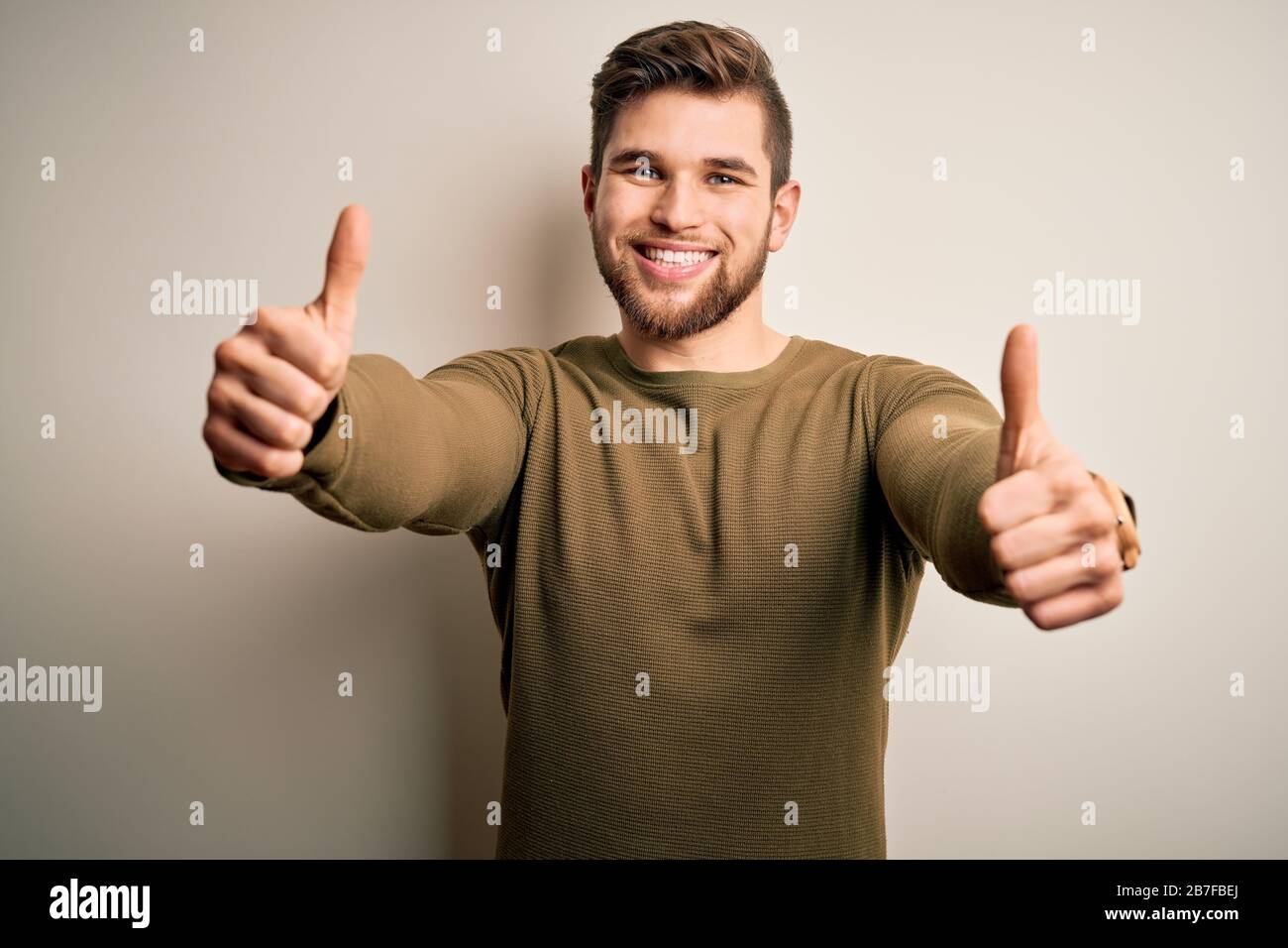 Young blond man with beard and blue eyes wearing green sweater over ...