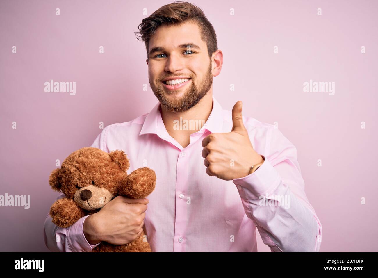 Young blond man with beard and blue eyes holding teddy bear toy over ...