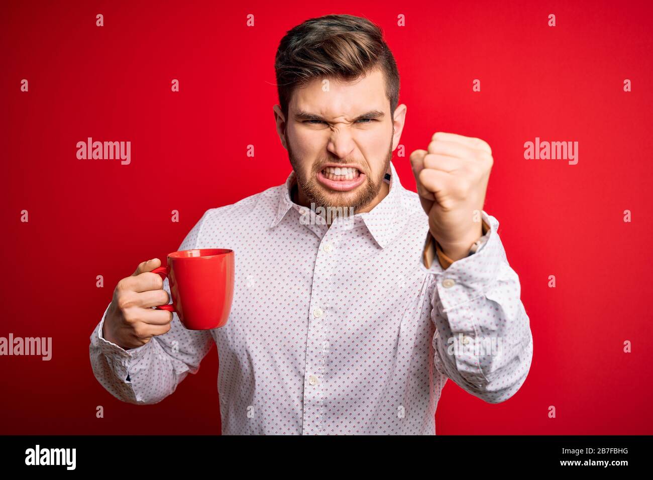 Young blond businessman with beard and blue eyes drinking red cup of ...