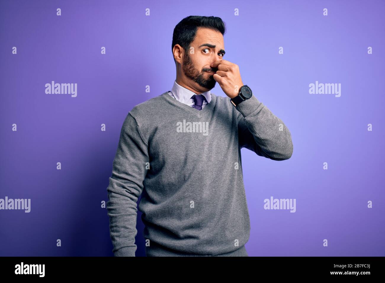 Handsome businessman with beard wearing casual tie standing over purple ...