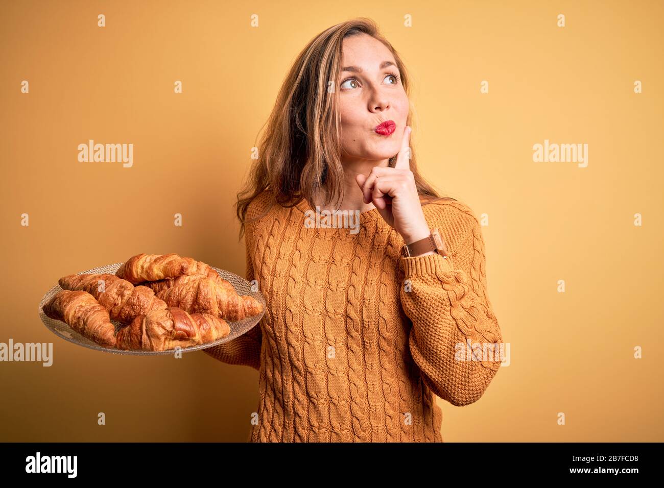 Young beautiful blonde woman holding plate with croissants over ...