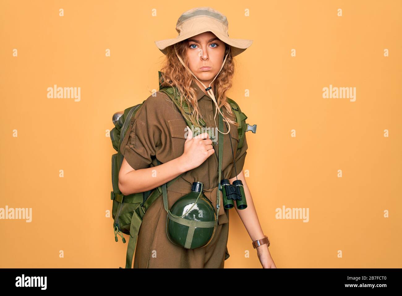 Young blonde explorer woman with blue eyes hiking wearing backpack and ...