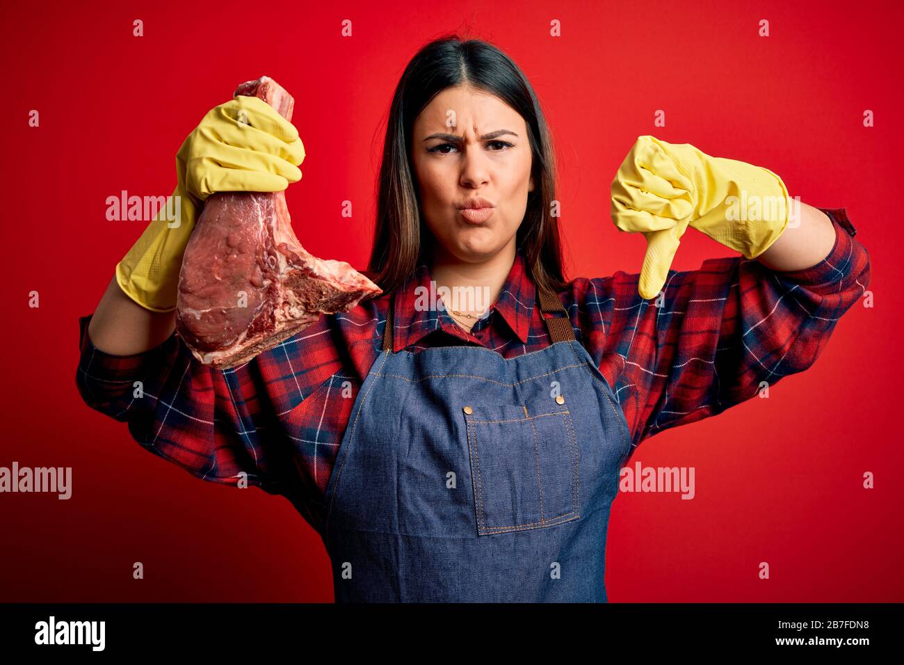 Young butcher woman holding fresh raw beef meat stake over red ...