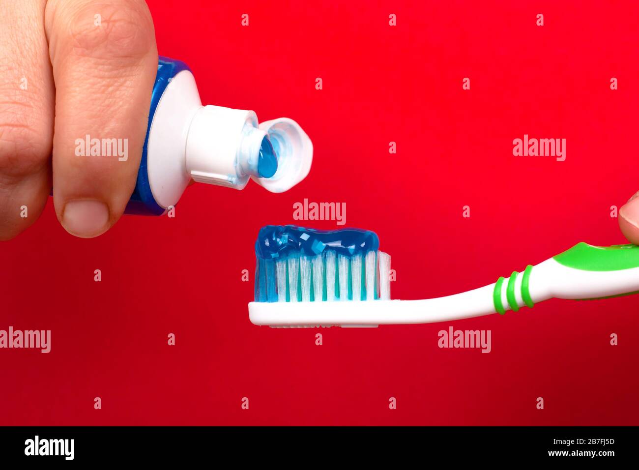 hand squeezes toothpaste on a toothbrush on a red background close-up ...