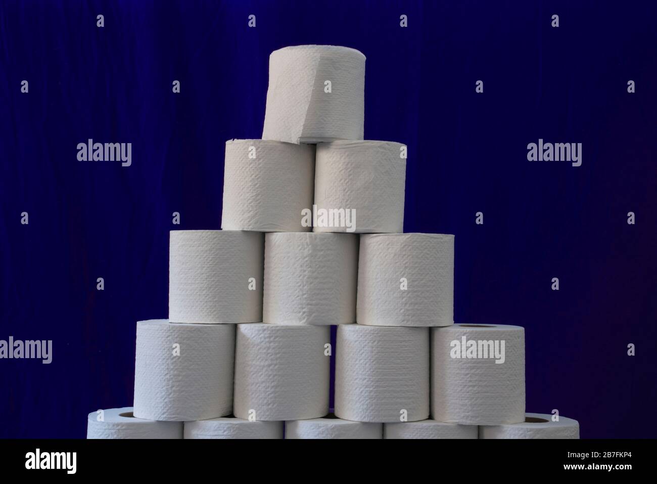 Toilet paper roll stacked in an organized pyramid against a blue ...