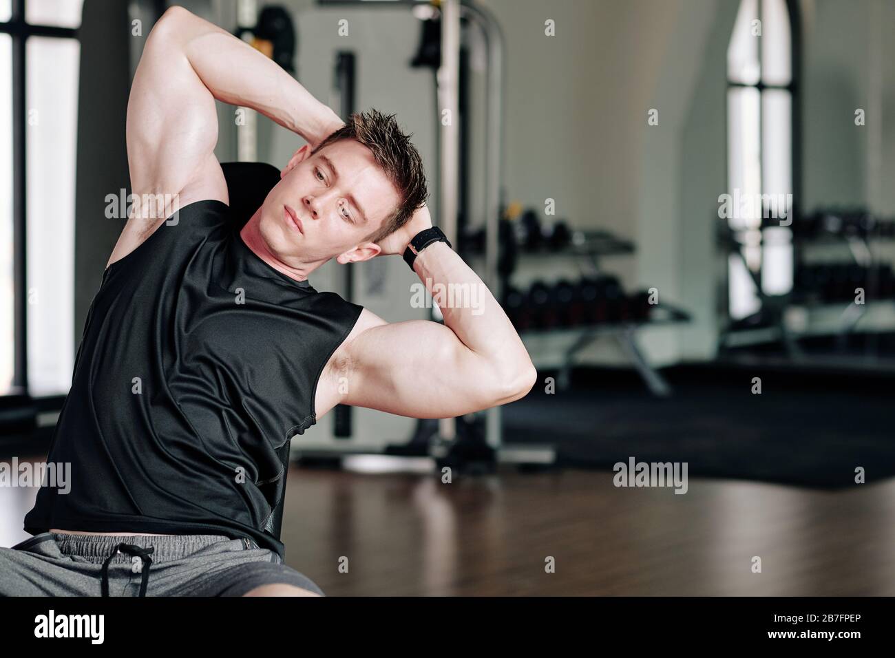 Serious handsome young man doing side bends when working out in gym ...