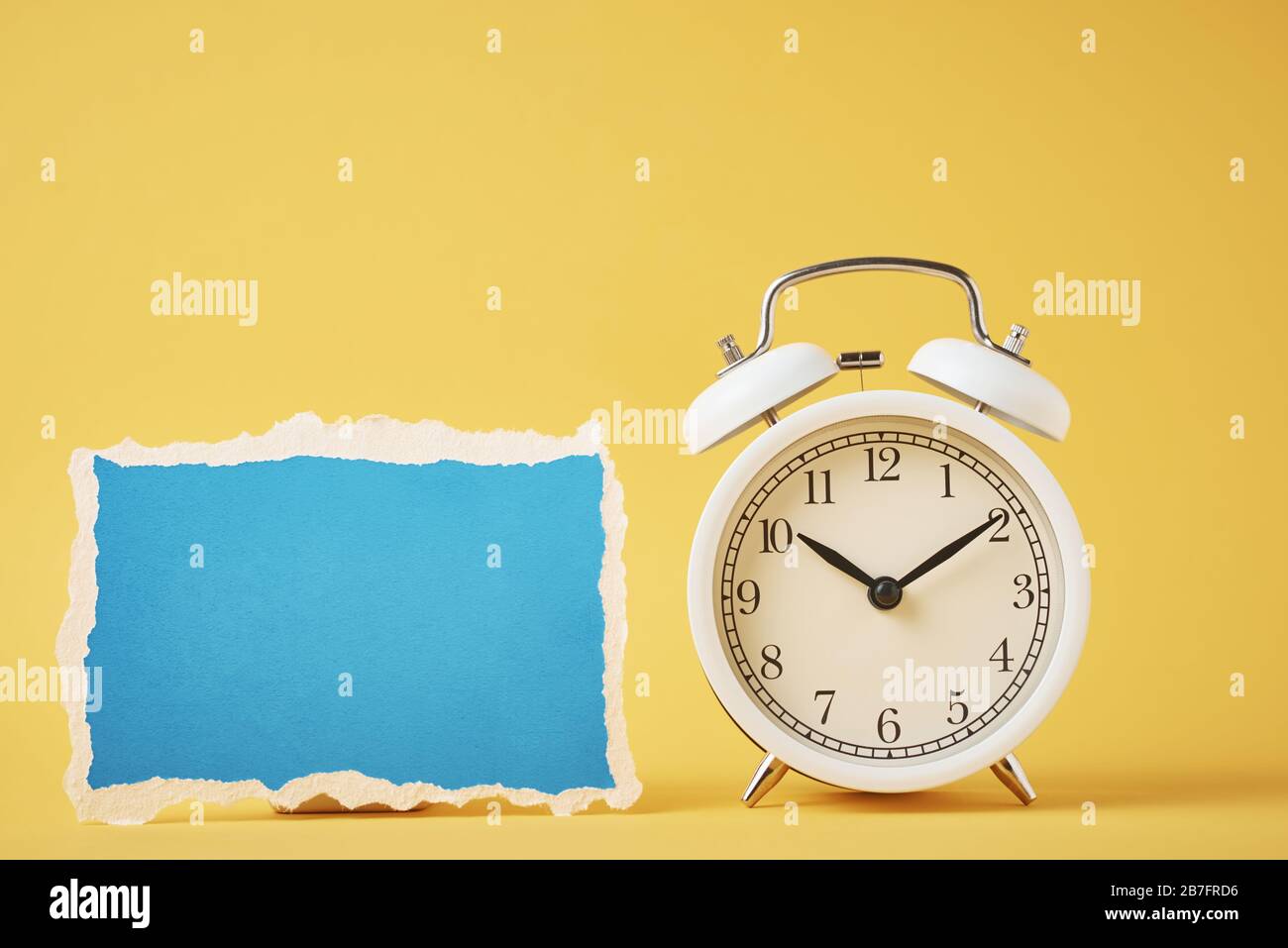White vintage classic alarm clock with bells and empty blue torn paper ...