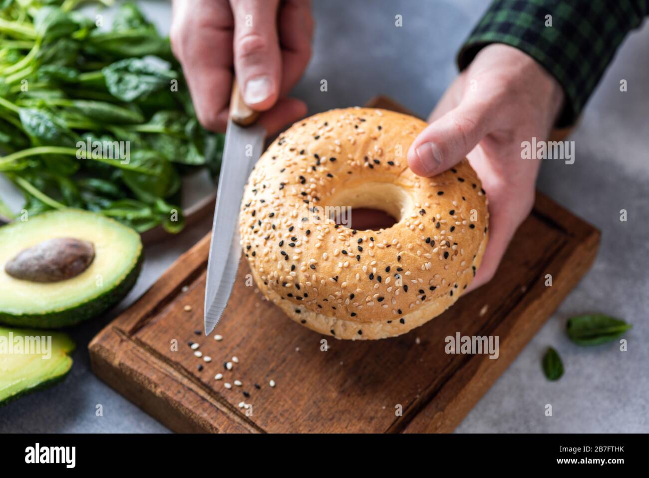 Person cutting bagel in halves with knife. Sesame bagel in male hands ...