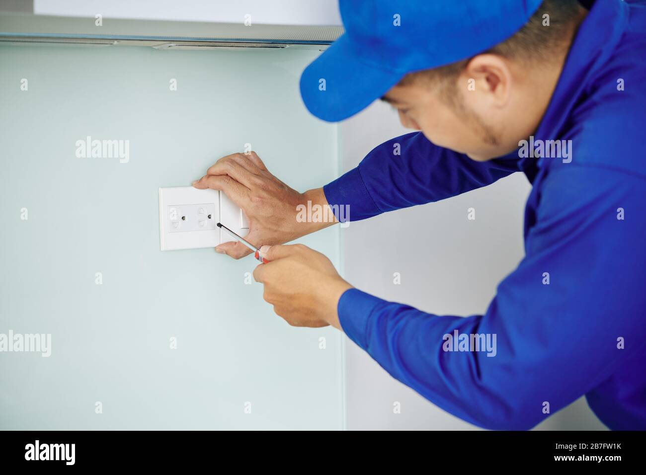 Professional electrician in blue uniform installing power socket with ...