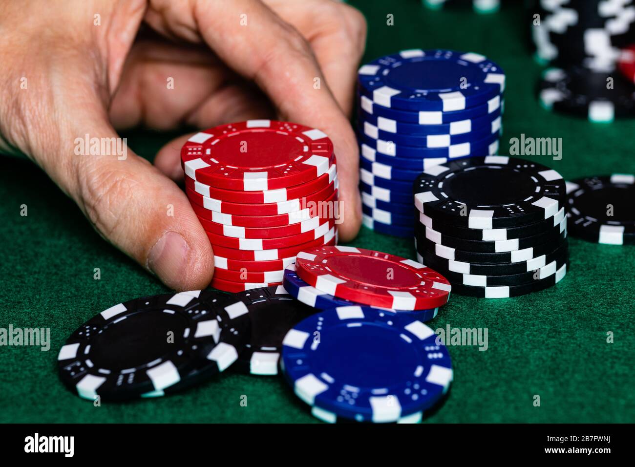 A Caucasian male hand placing a stack of red betting chips into the pot ...