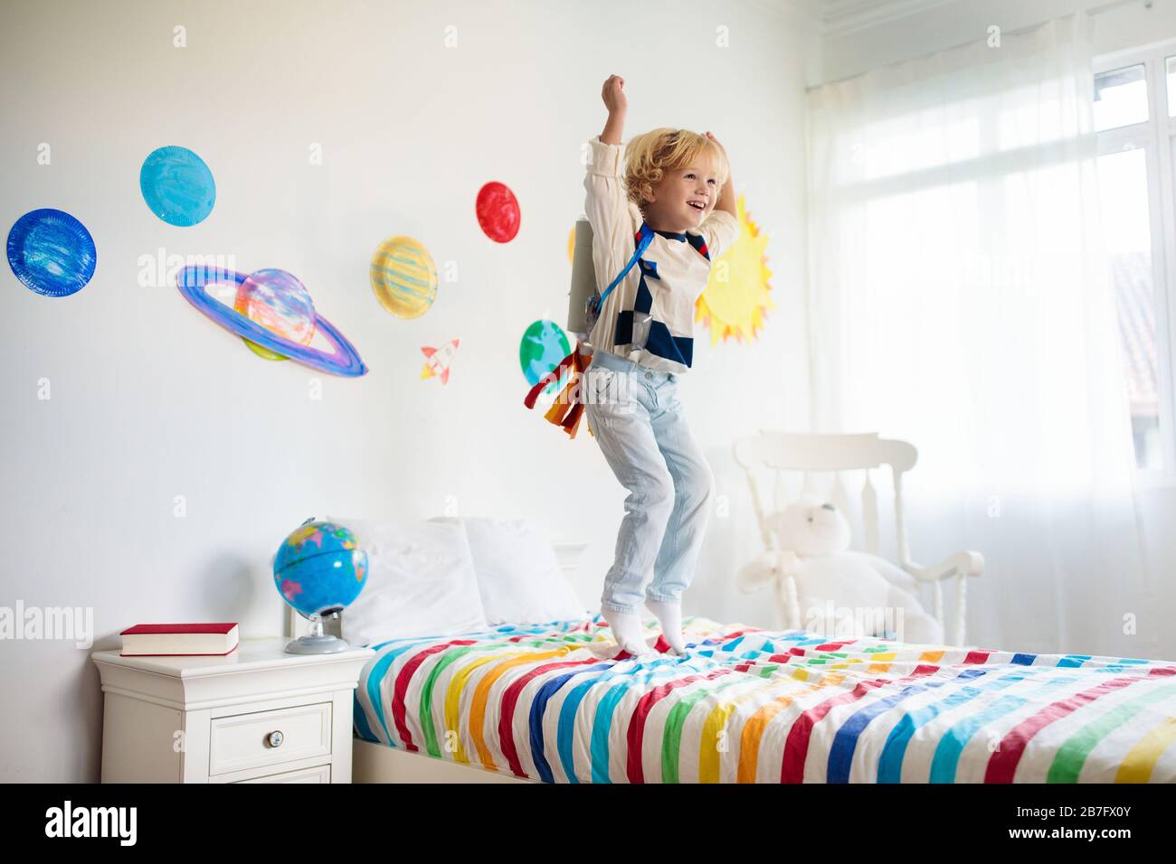 Kids play astronaut. Little boy in space costume jumping on bed with ...