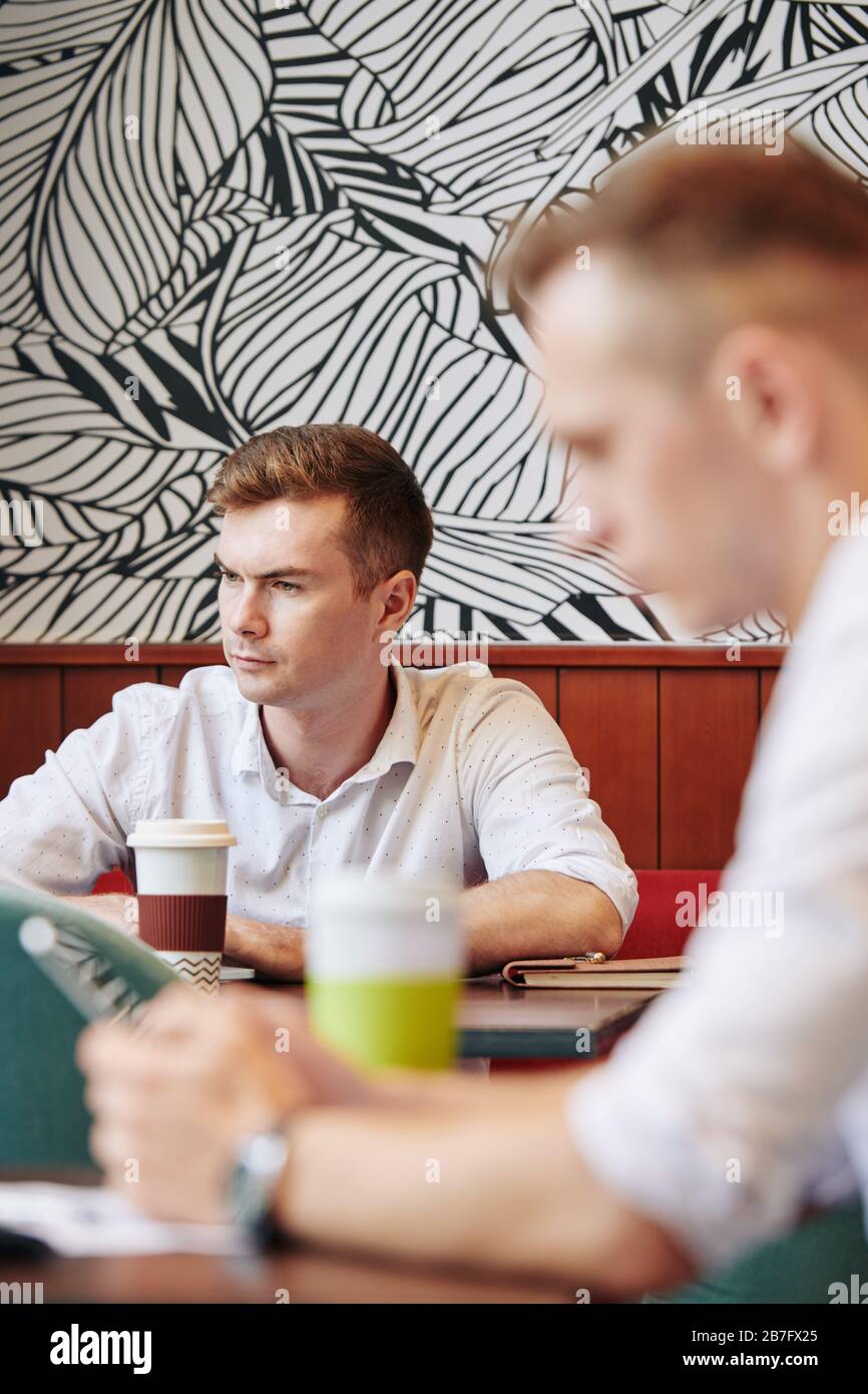 Serious frowning young businessman working on laptop at local cafe and ...
