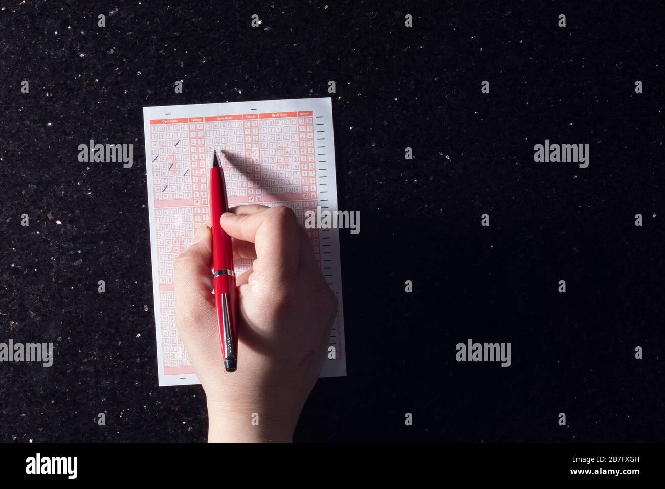 Person's hand filling in the checklists in a planner on a black surface ...