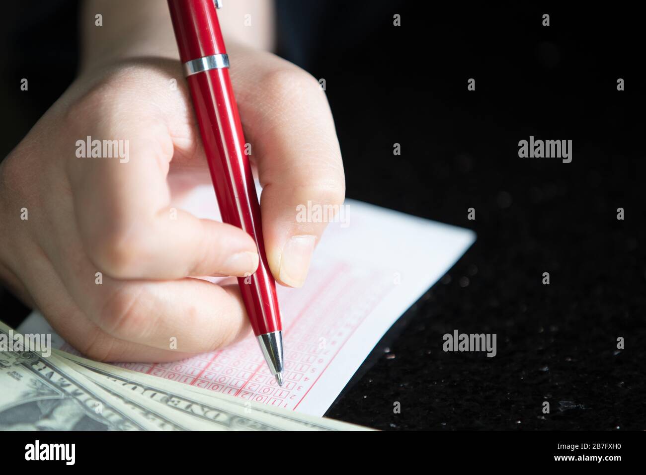 Person's hand filling in the checklists in a planner on a black surface ...