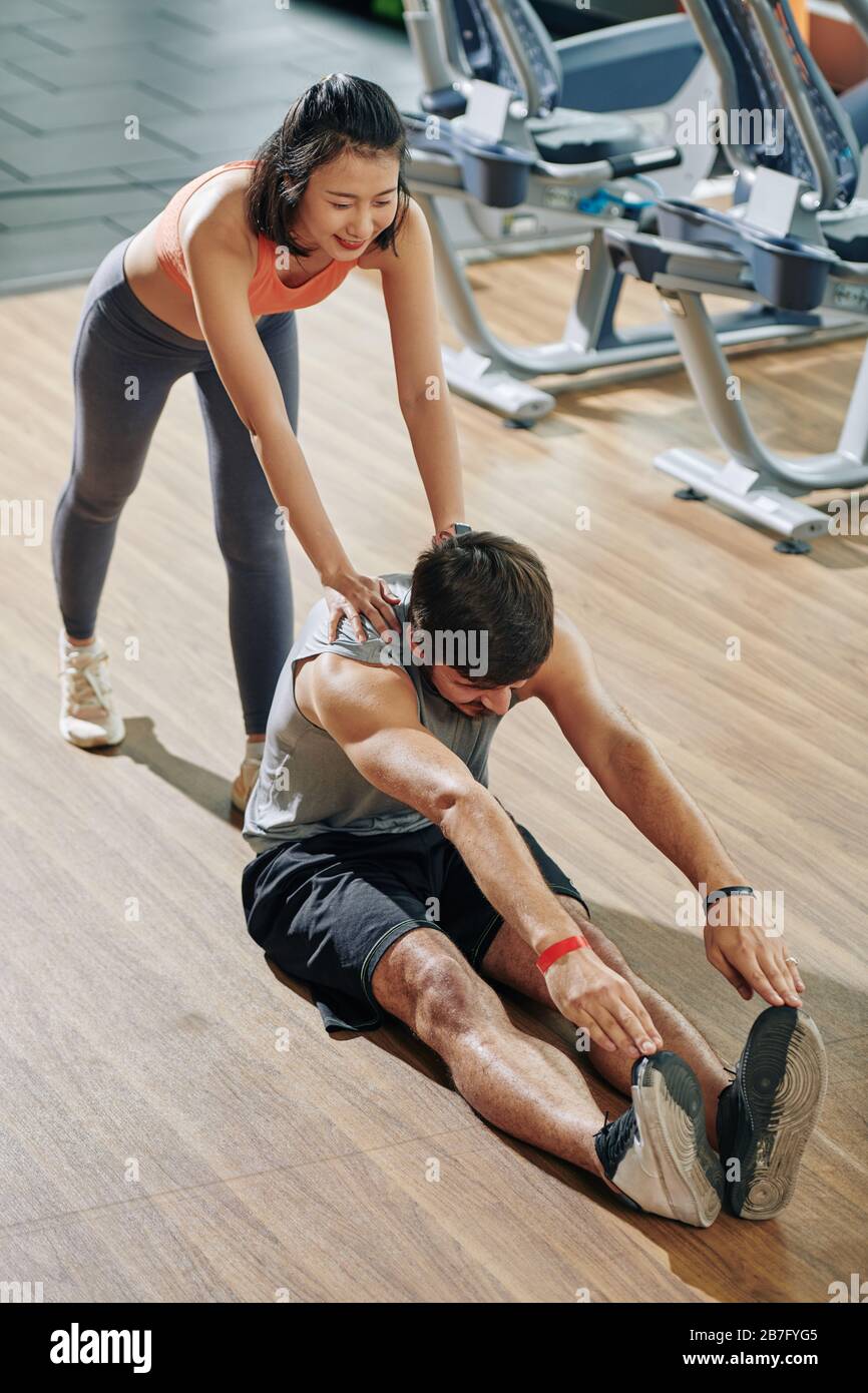 Smiling female fitness trainer pushing back of her client reaching to ...