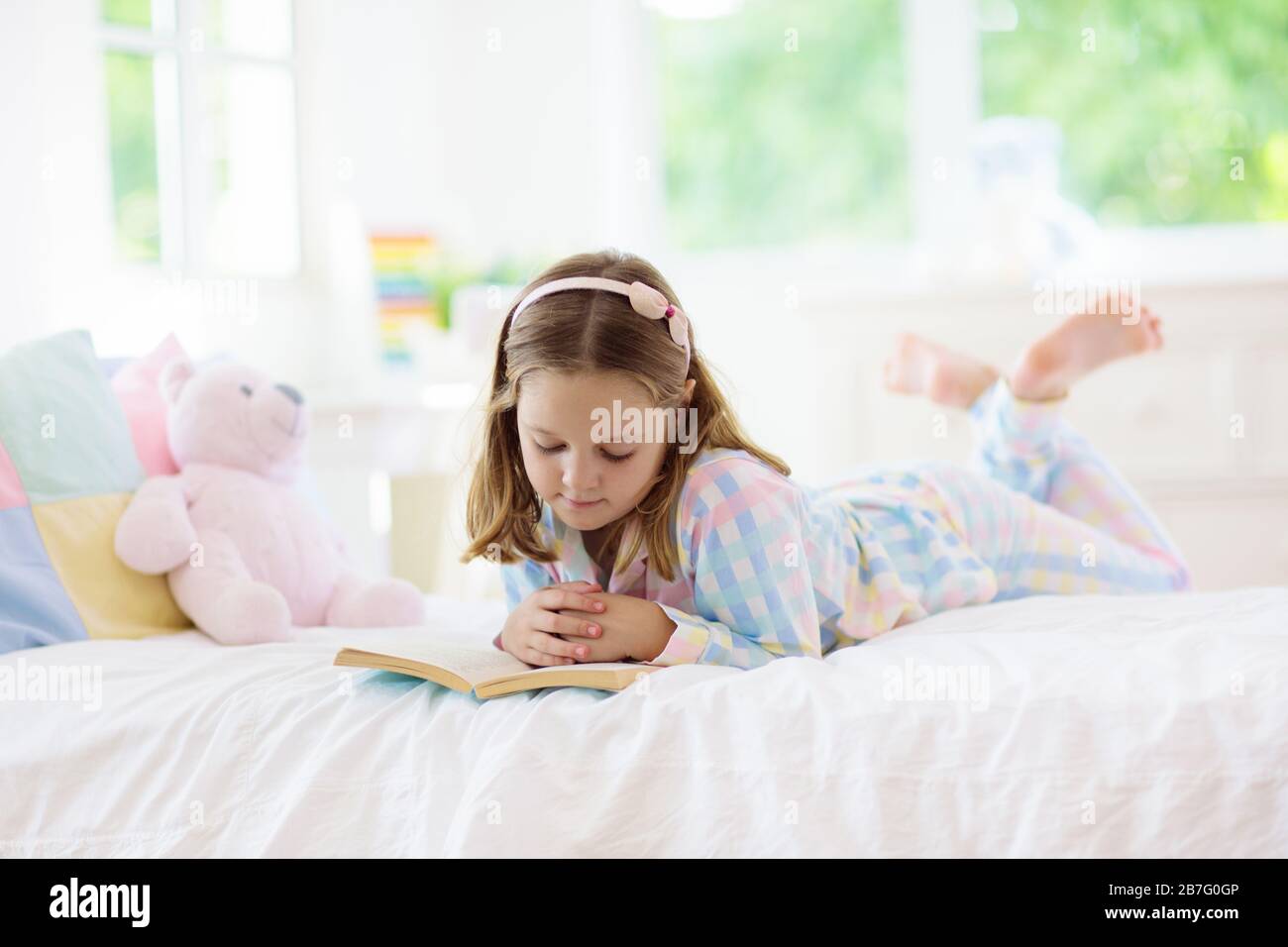 Child reading book in bed in white sunny bedroom with window. Children ...