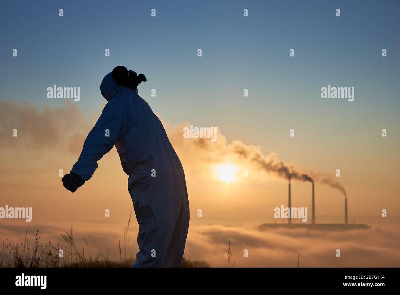 Side view of scientist in gas mask. Blue sky over power plant on ...