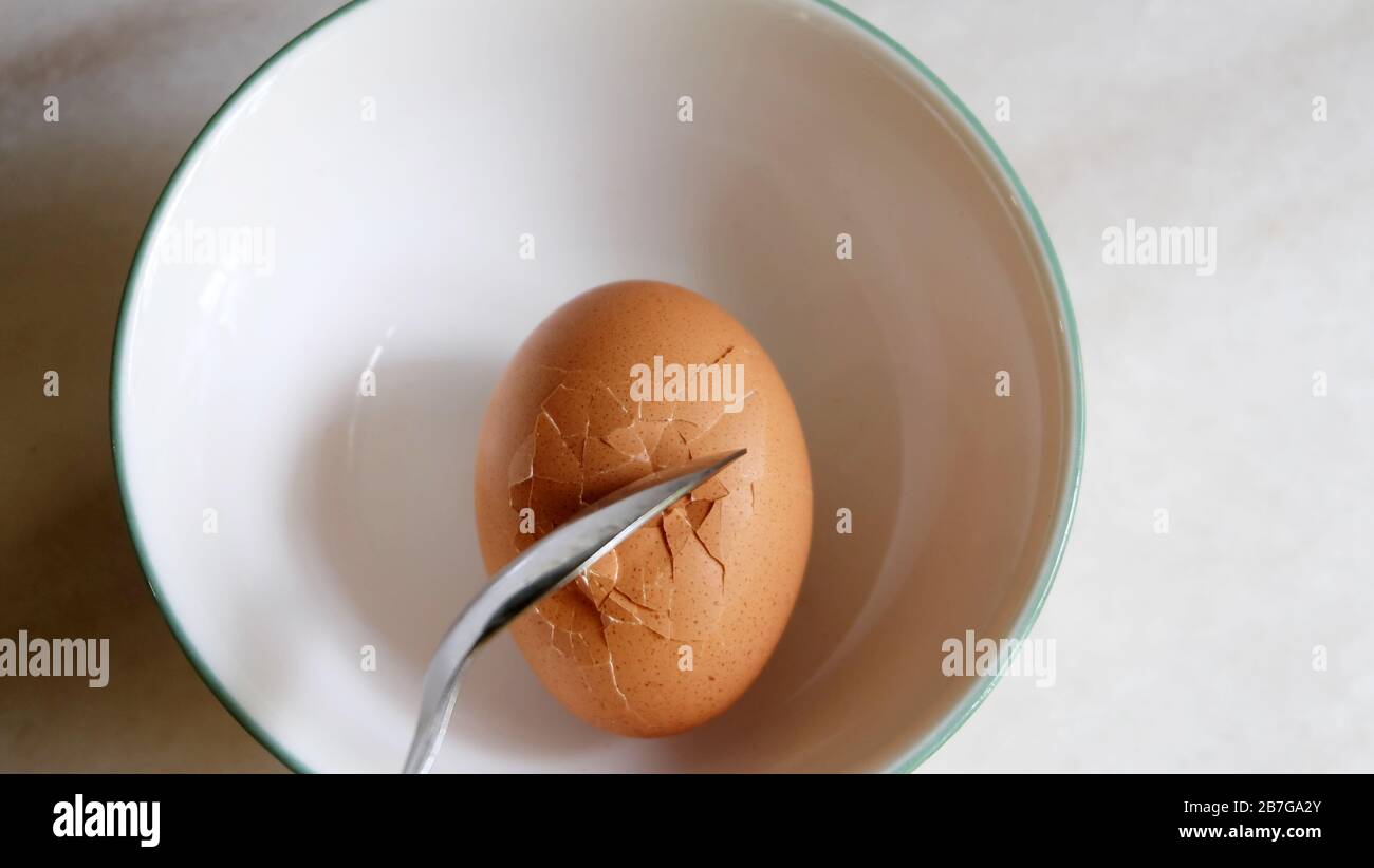 A brown egg inside a bowl, with a silver spoon hitting it and causing ...