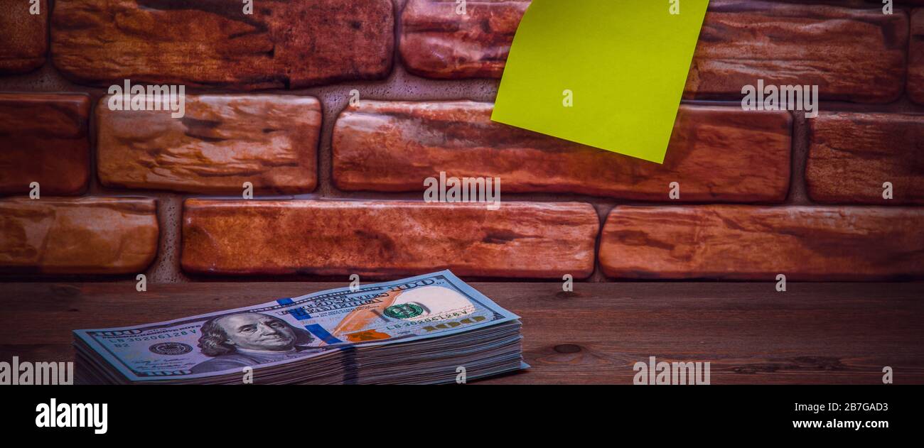 A stack of hundred-dollar bills against a brick wall and a note Stock ...