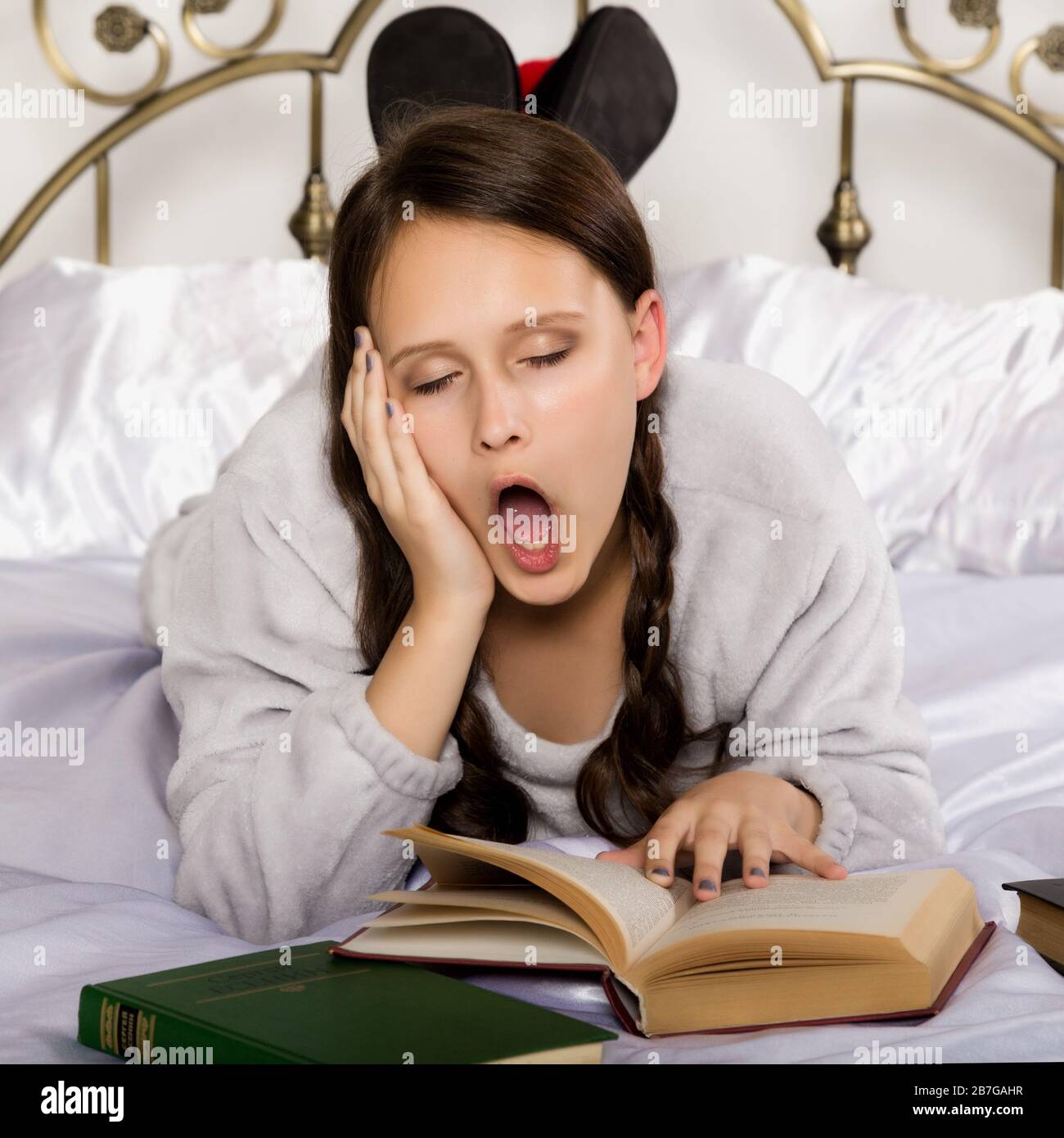 sad young student girl reads a book while lying on a bed doing homework ...