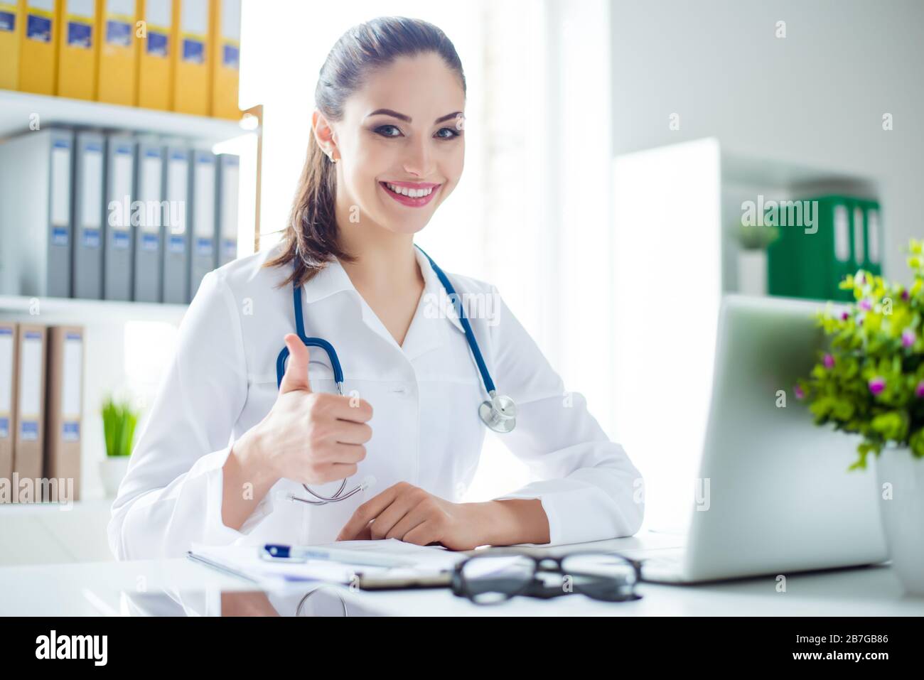 Smiling glad doctor at her medical office sitting at the table and ...