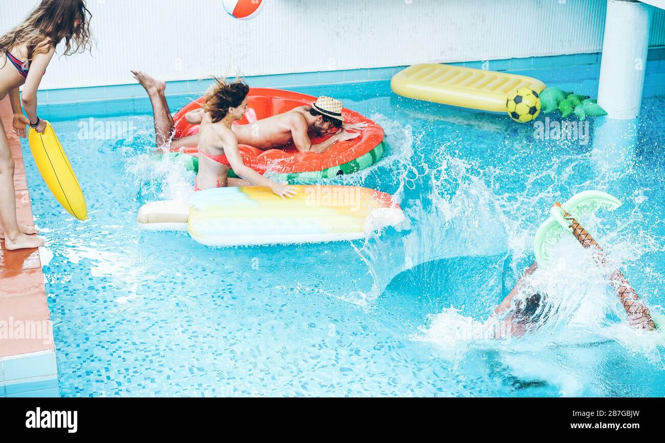 Happy friends jumping inside swimming pool with tropical fruits lilos ...