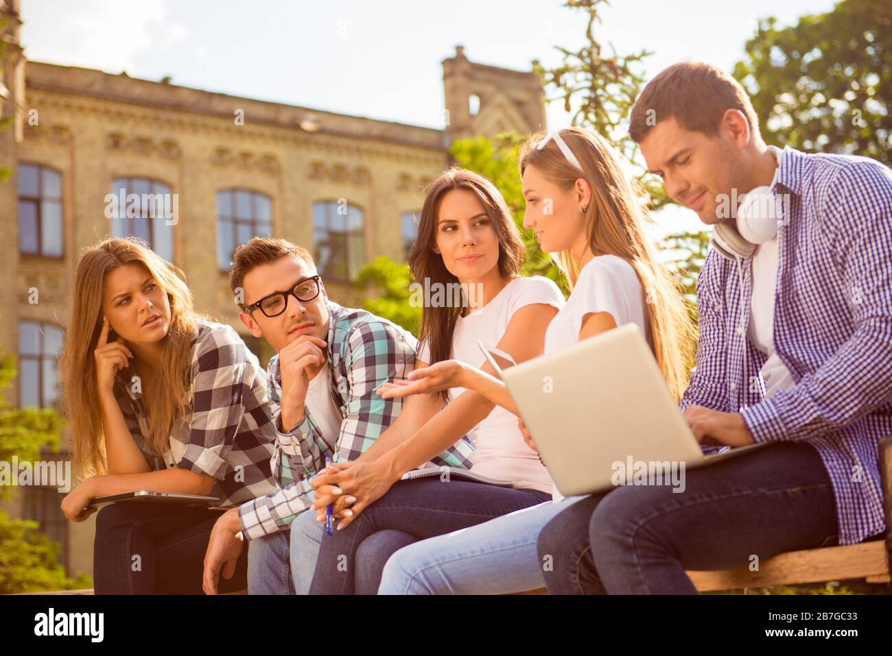Group of five happy students sitting on bench and talking Stock Photo ...