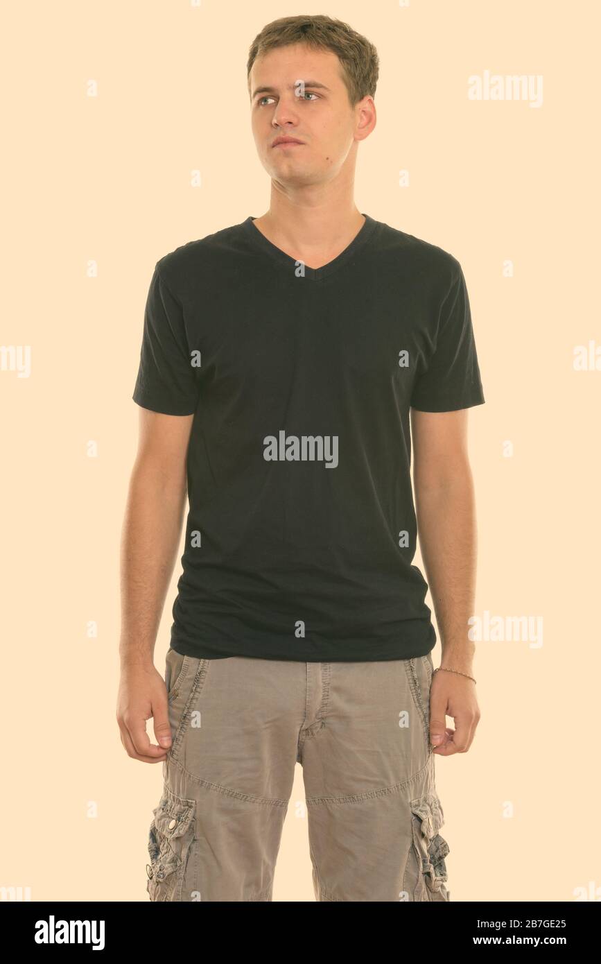 Studio shot of young man standing and thinking while looking at ...