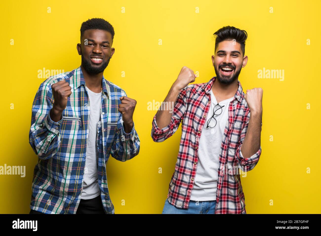 Portrait of a two satisfied young men celebrating isolated over yellow ...