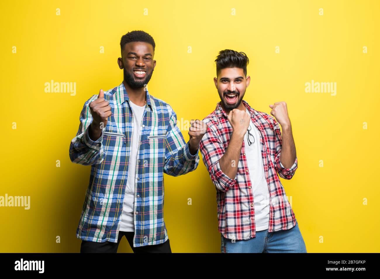 Portrait of a two cheerful young men celebrating isolated over yellow ...