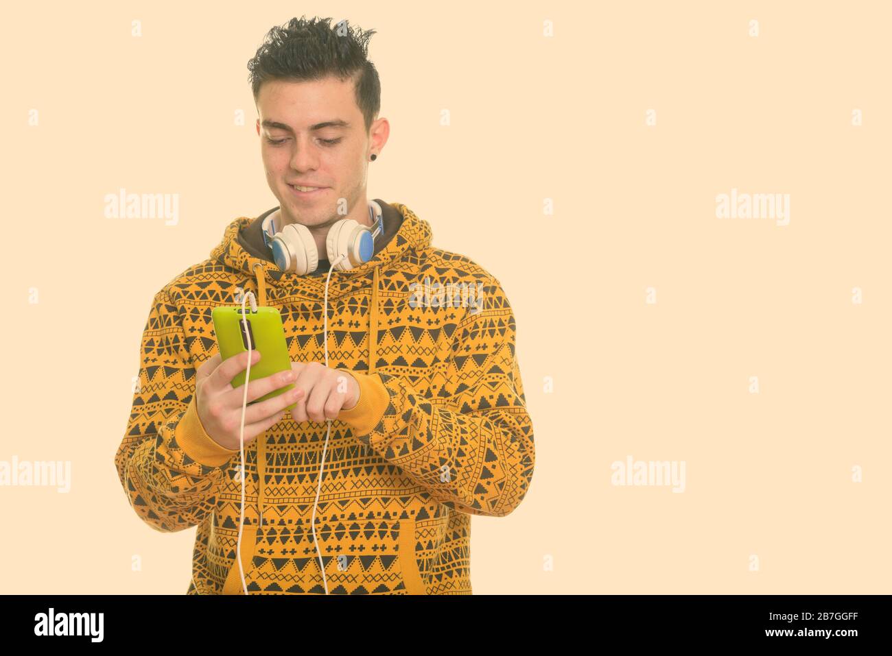 Happy young man smiling and using mobile phone while wearing headphones ...