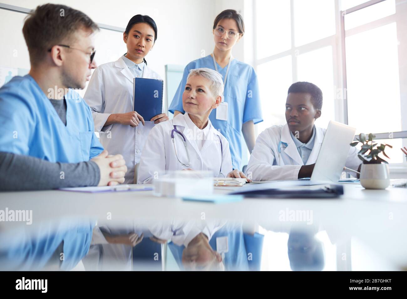 Multi-ethnic group of doctors working together sitting at desk in ...