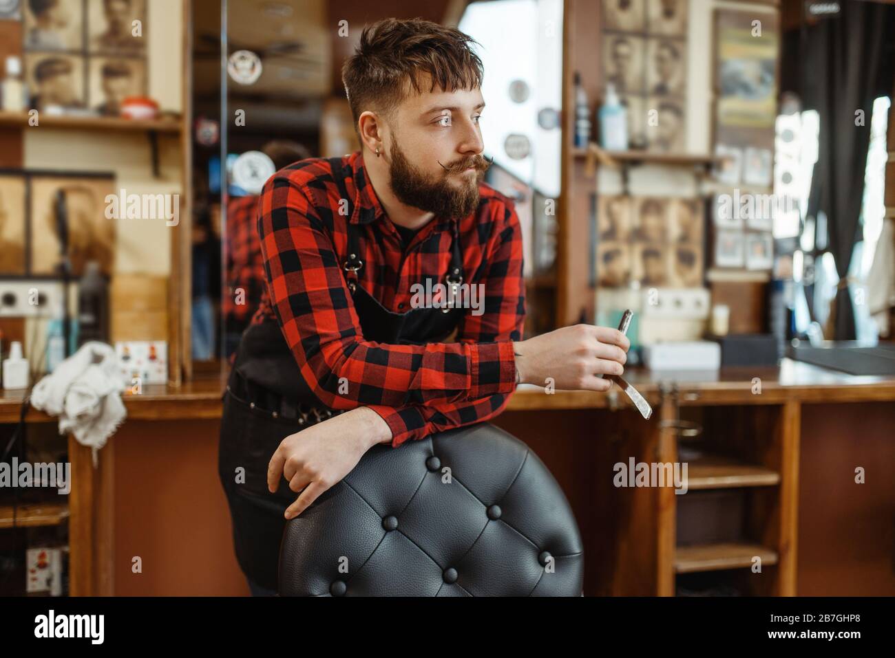 Barber with razor poses at the chair, barbershop Stock Photo - Alamy