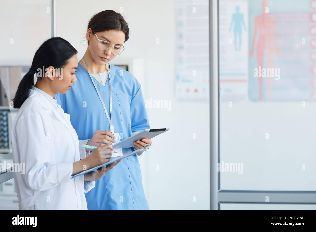 Side view portrait of two female medics filling forms while standing in ...